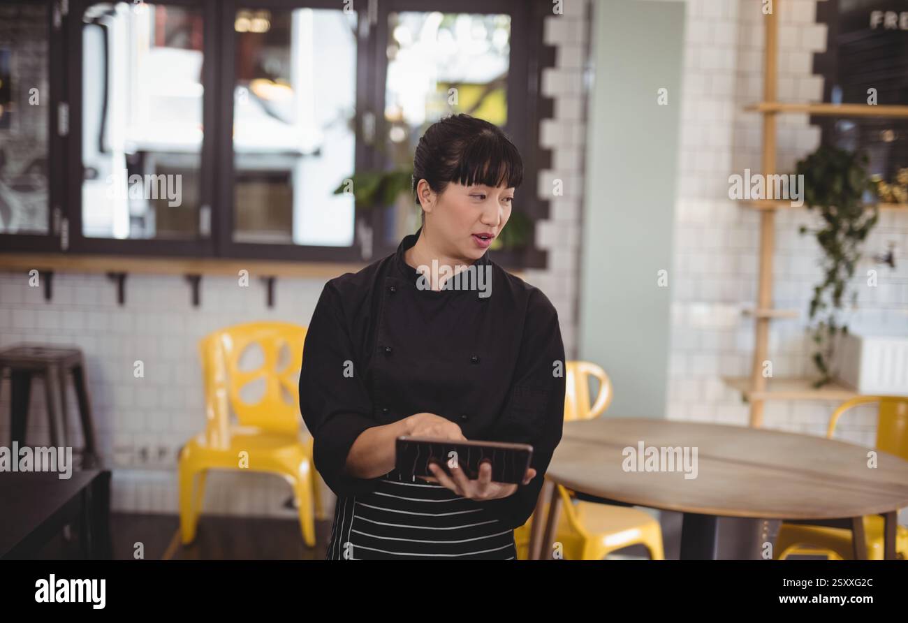 Chef in modern cafe using digital tablet, planning menu with focused ...