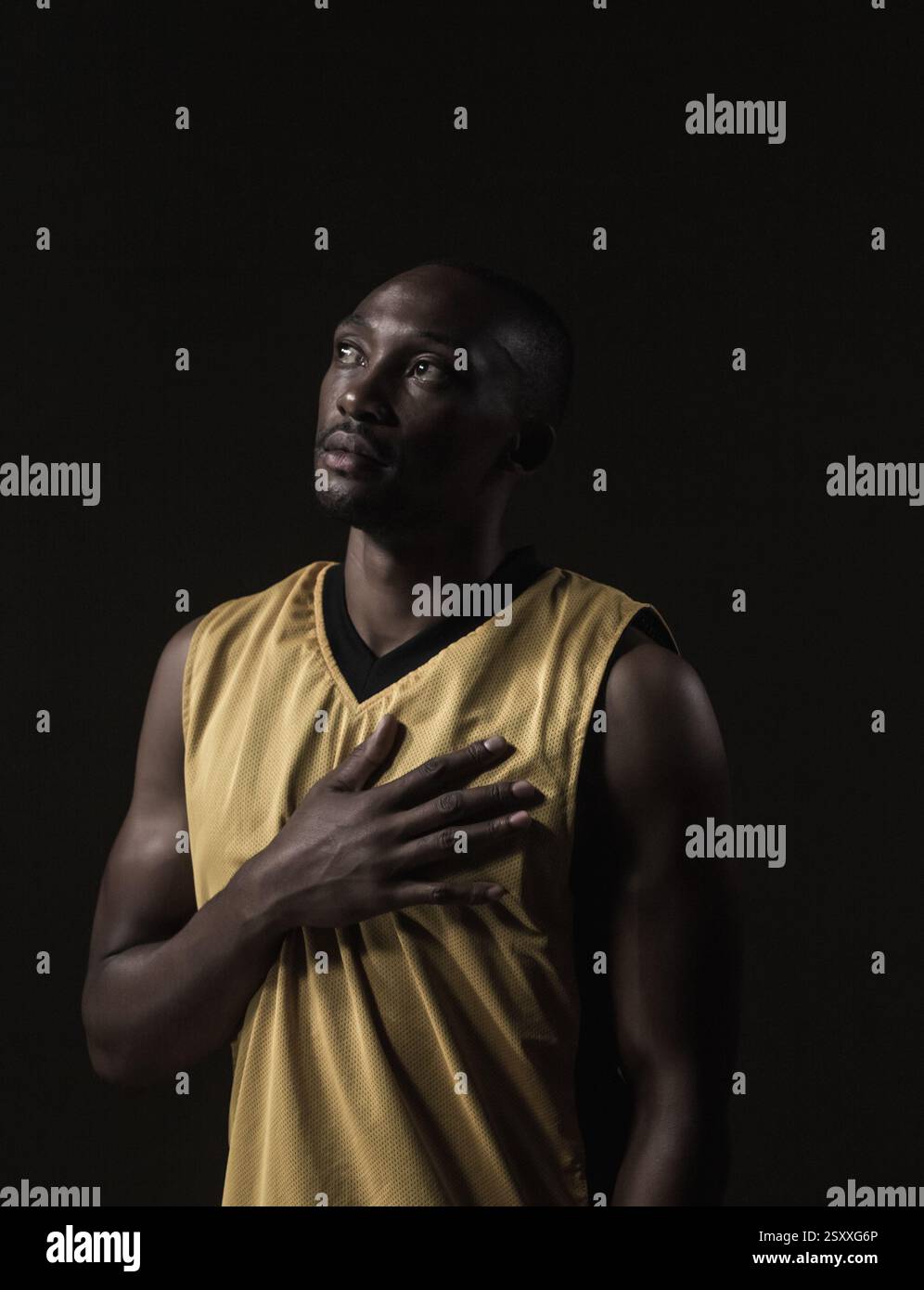 Basketball player in yellow jersey looking up, hand on chest ...