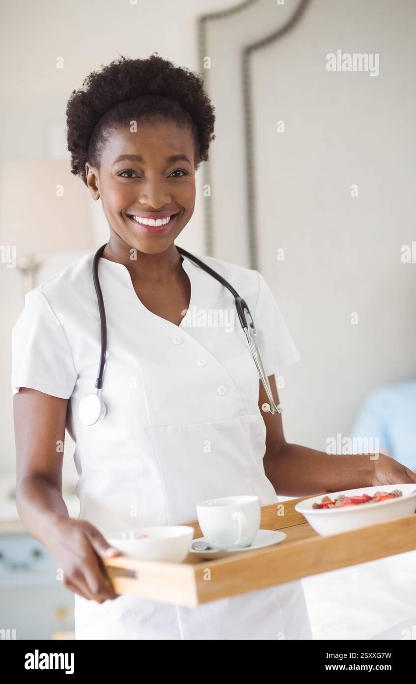 Smiling nurse carrying breakfast tray with coffee and fruit in hospital ...