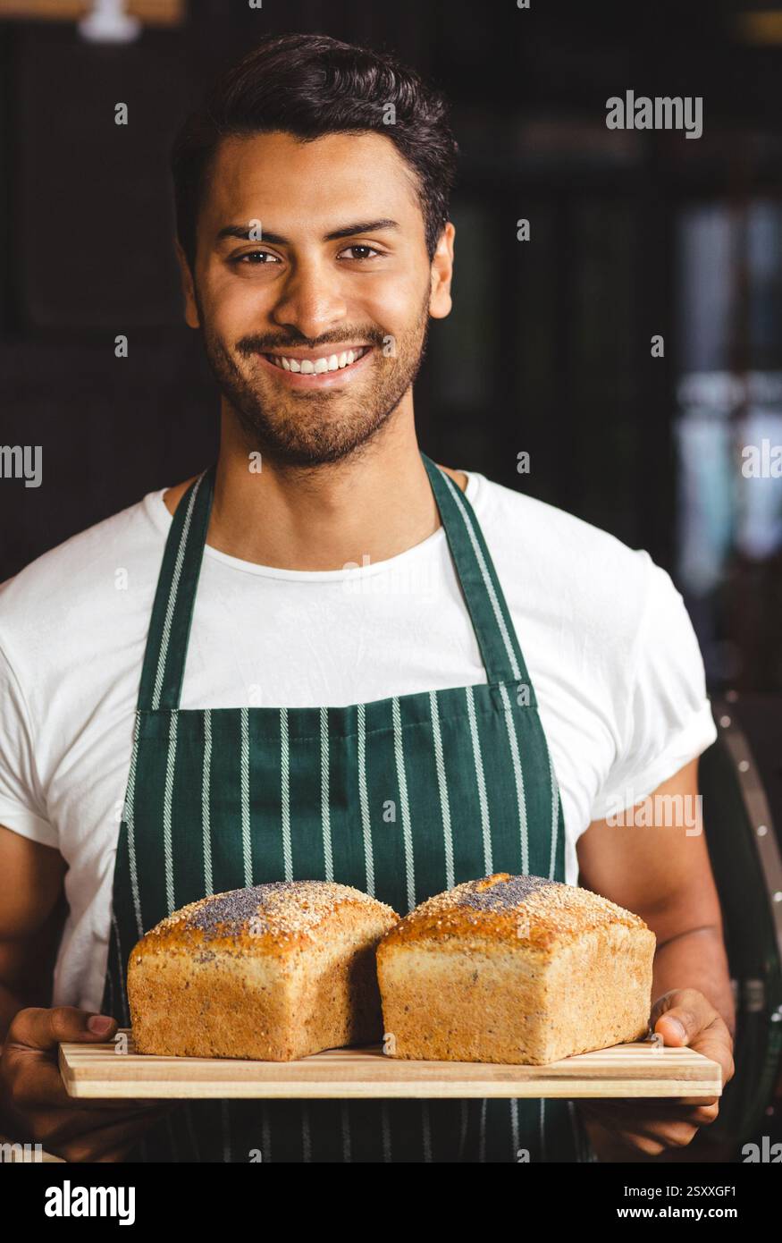 Smiling man holding freshly baked bread in coffee shop, wearing striped ...