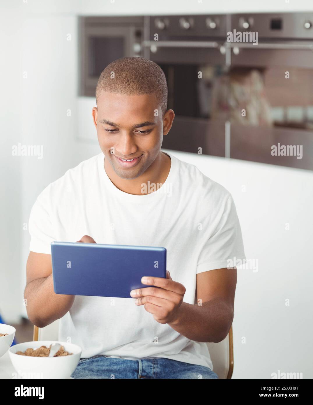 Smiling man using tablet while enjoying breakfast in modern kitchen ...
