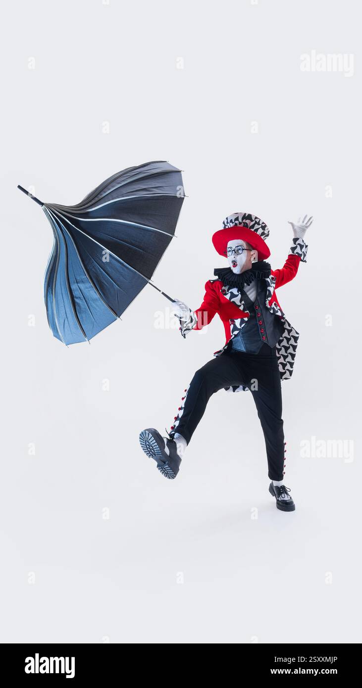 Expressive mime performer balancing with umbrella, exaggerated facial ...