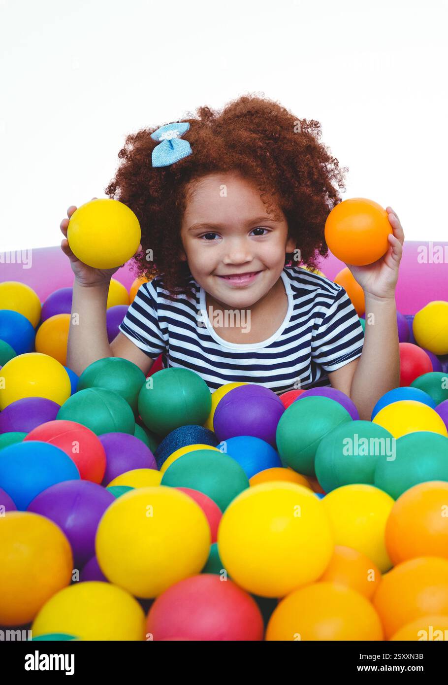 Smiling girl playing in colorful ball pit, holding yellow and orange ...