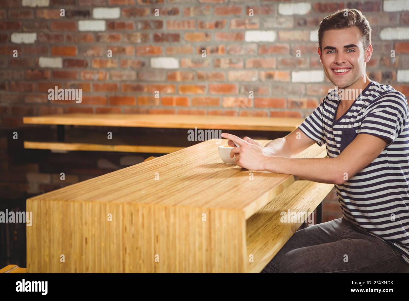 Smiling man enjoying coffee at rustic cafe with brick wall background ...