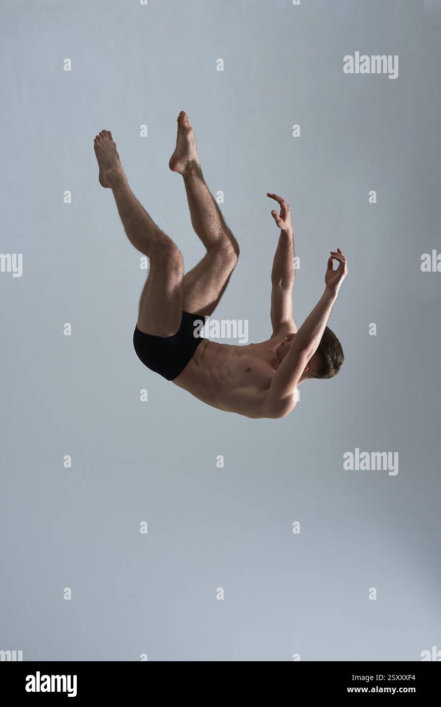 A male dancer in black shorts is captured mid-air in a falling motion ...
