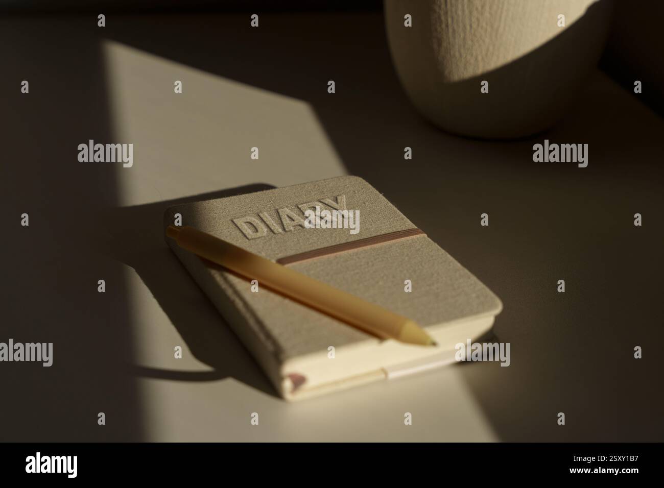 A textured diary with a yellow pen resting on it, placed on a white ...