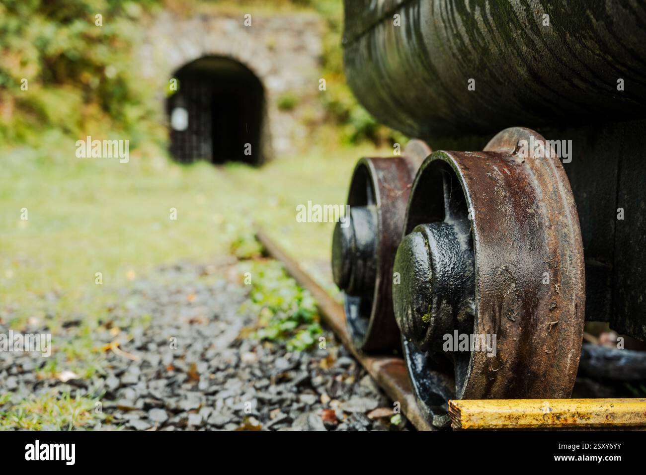 Rusty mining truck wheels rest on gravel beside an old tunnel entrance ...