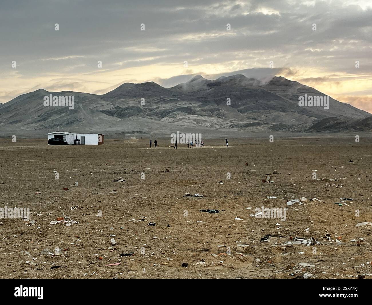 Unrecognisable bunch of kids playing soccer in desert by sunset. Dry coast of Peru with ...