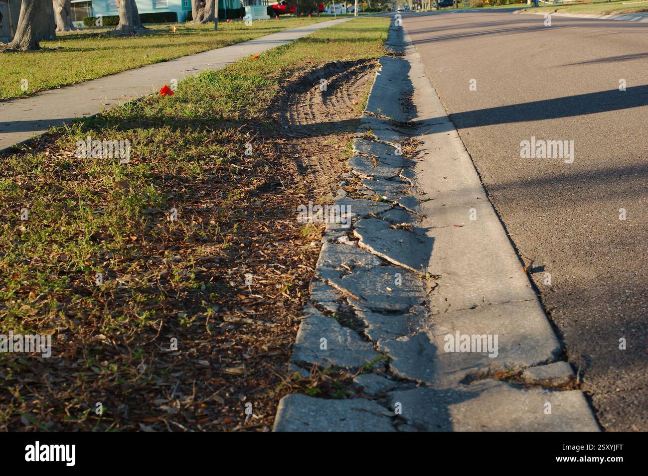 Wide leading line view down a broken concrete gutter beside the street ...