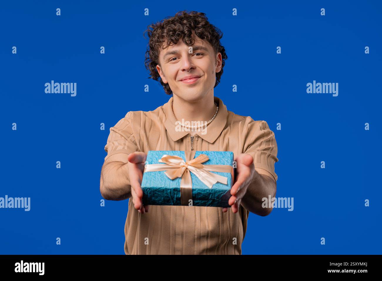 Man gives gift box by hands to camera on blue background. Guy smiling ...
