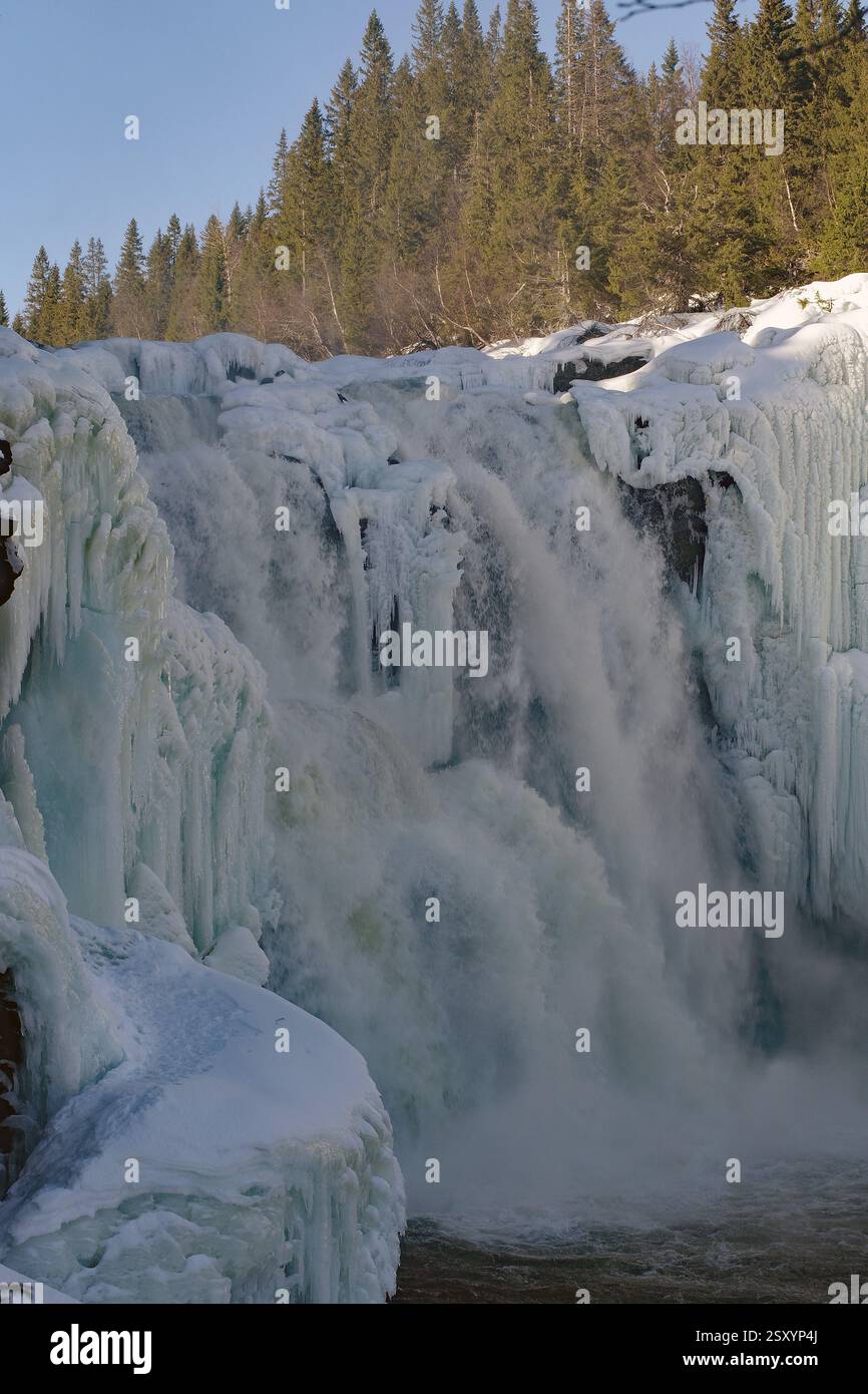 A frozen waterfall with forest in the background and snow on the rocks ...