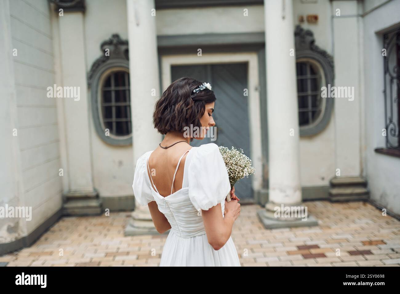 Rear view. Holding flowers. Bride in dress is outdoors before her ...