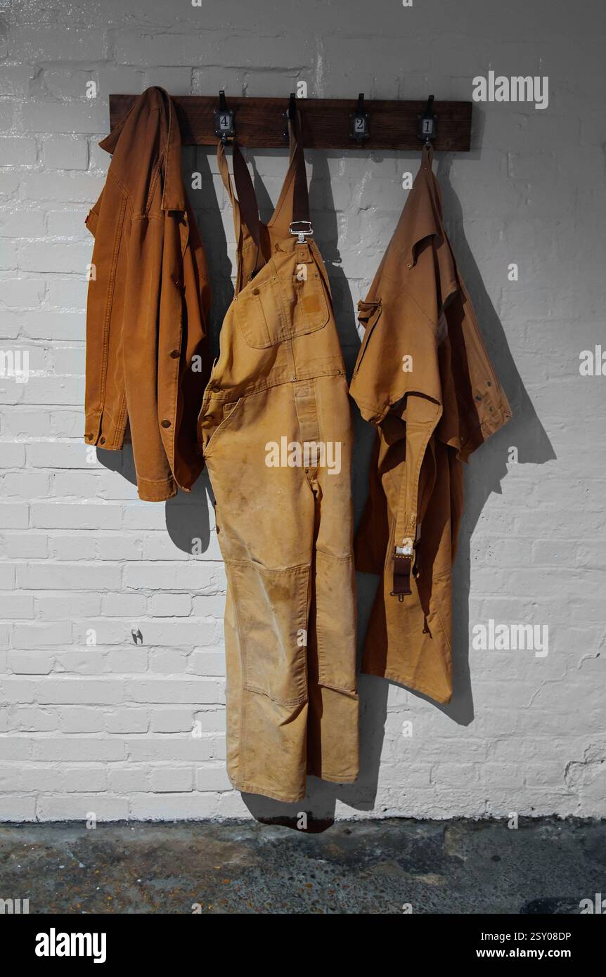 Vintage Overalls And Work Clothes Hanging On Pegs Against A White ...