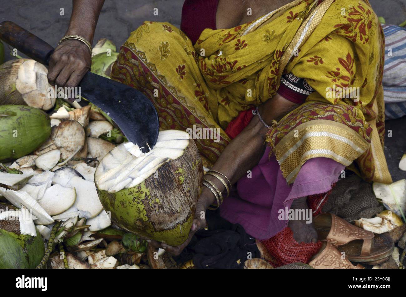 Lady vendor cutting coconut with sickle on road side at Kolkata India ...