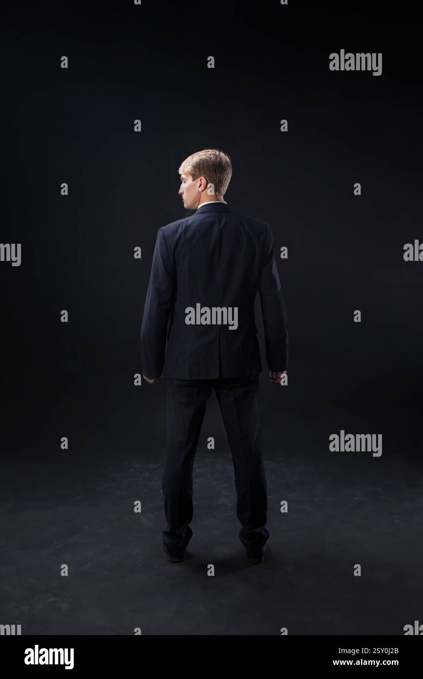 In a dark studio, a man stands confidently in a crisp black suit and ...