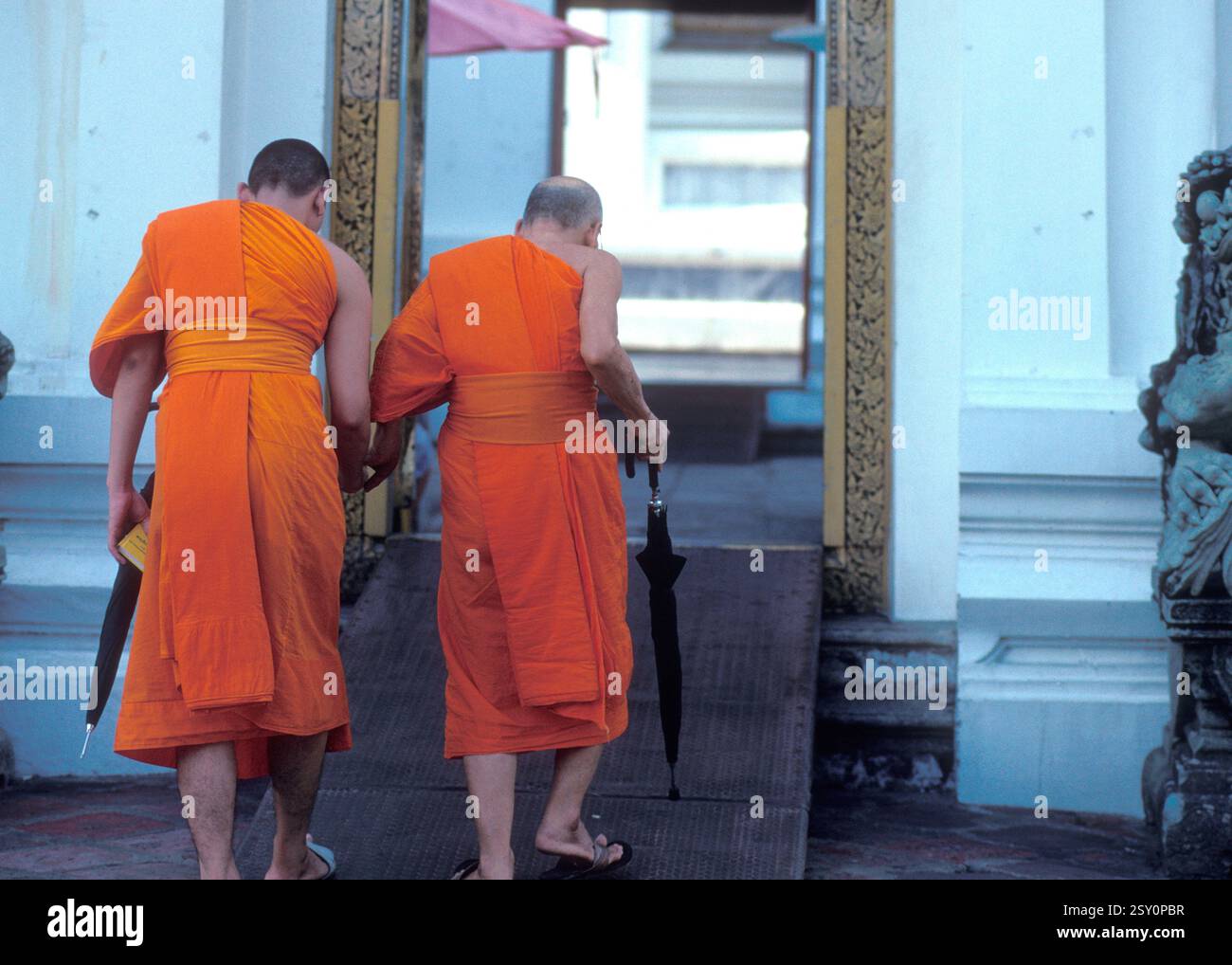 A pair of elderly Buddhist monks in bright orange robes walking into a ...
