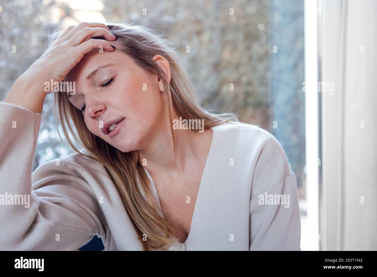 A woman with closed eyes rests her hand on her forehead, expressing deep melancholy and solitude ...