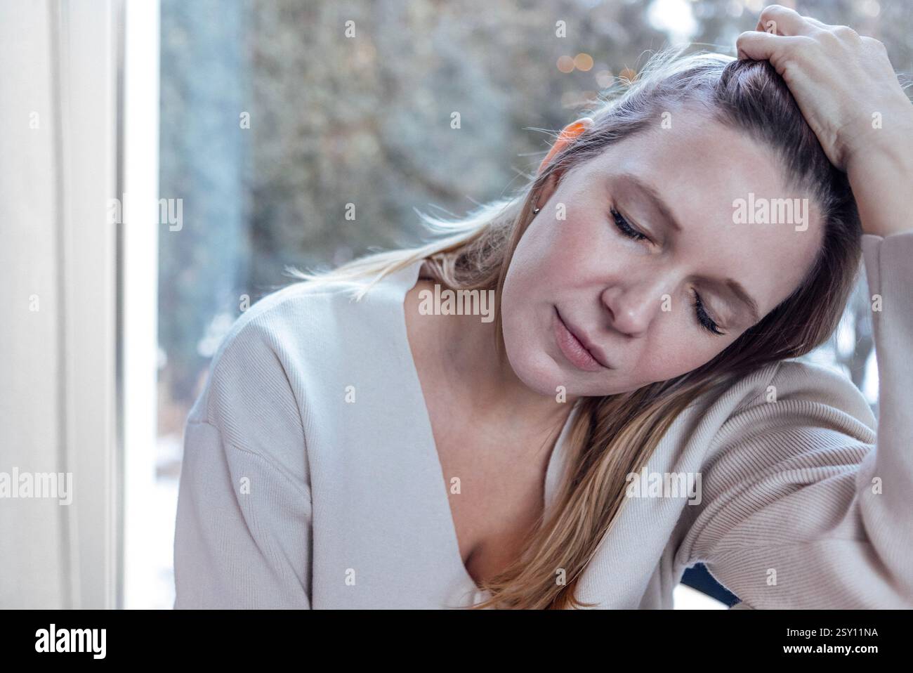 A woman leans against a window, eyes closed in contemplation and her ...