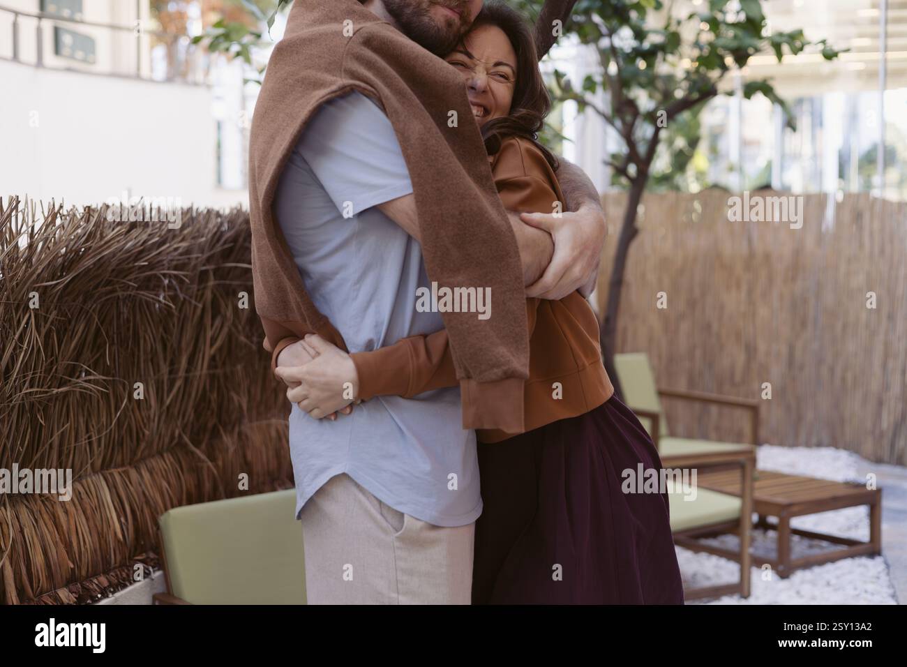 Man and woman share a warm embrace in a stylish outdoor area filled ...