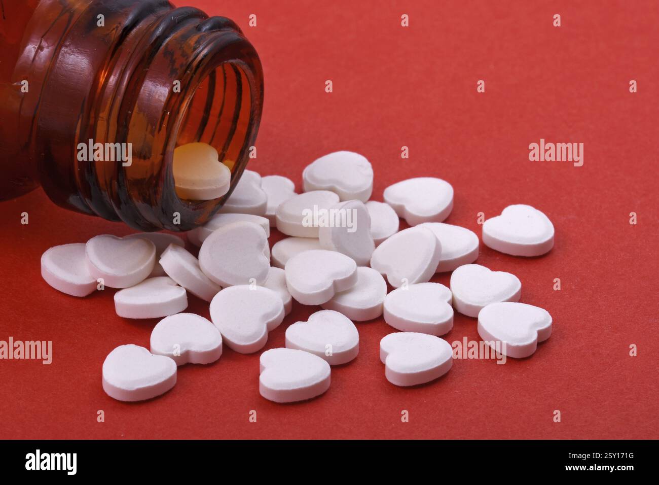 Heart shaped pills from bottle glass on a red background. Medicines ...