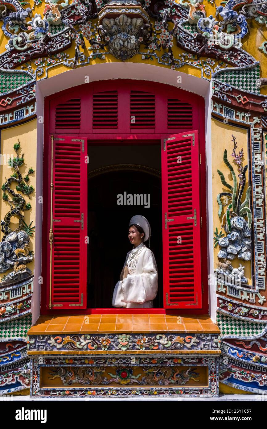 A young woman in traditional dress poses in a window of Kien Trung Palace, Äián Kiáºn Trung ...