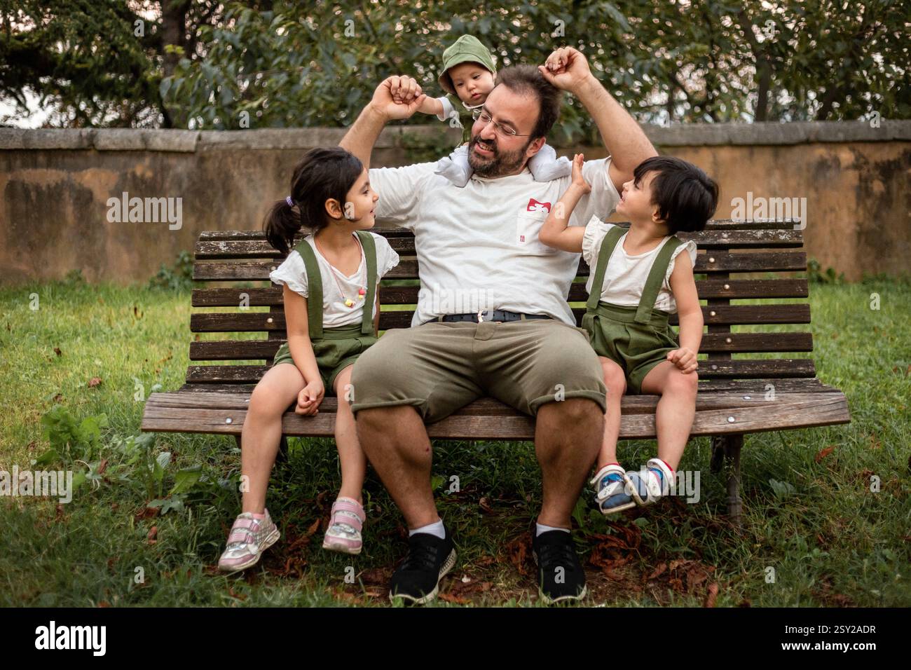 dad sitting with small baby and two elder daughters on the bench in the ...