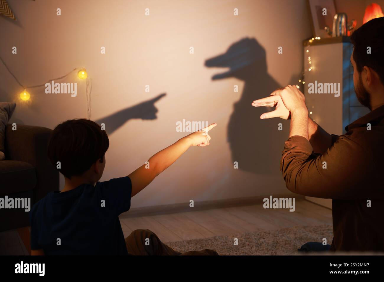 Father making hand gesture like duck while performing shadow play to ...