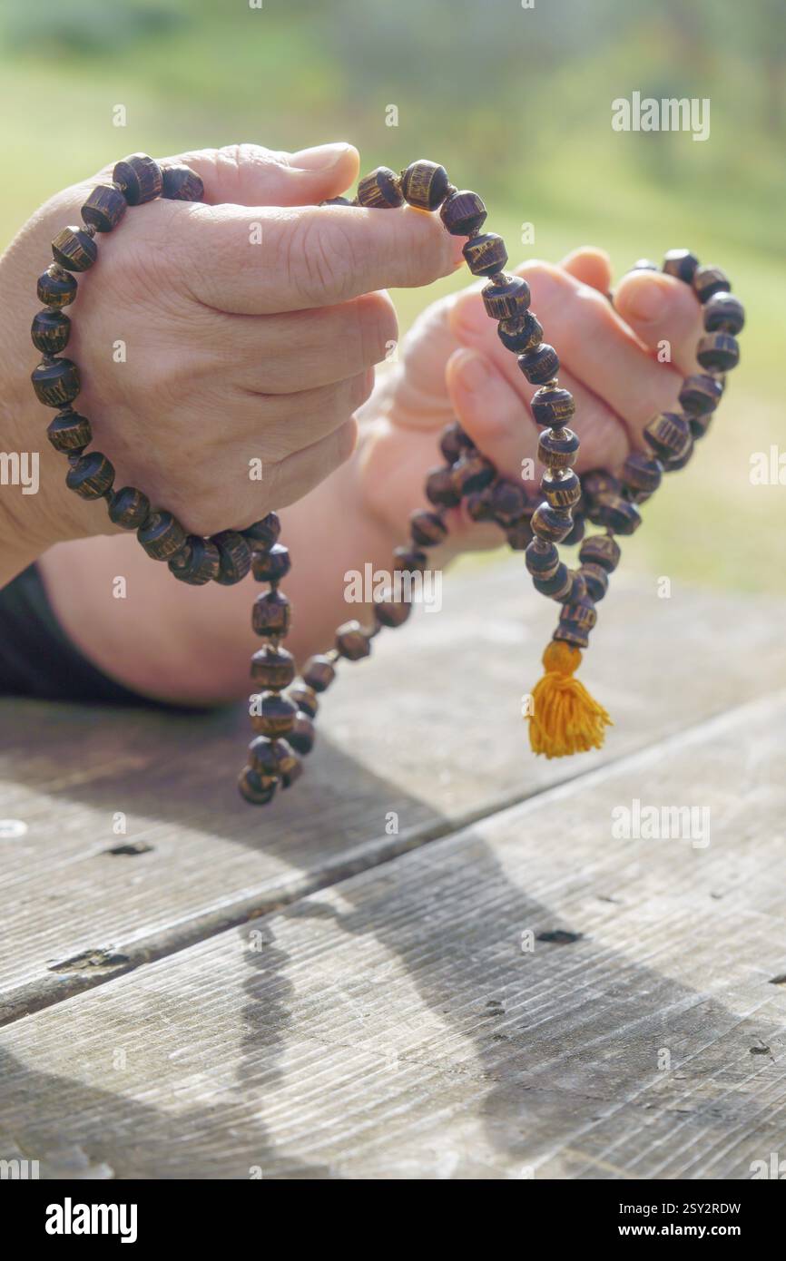 Close-up of a woman praying with a sunlit Buddhist wooden mala beads in ...