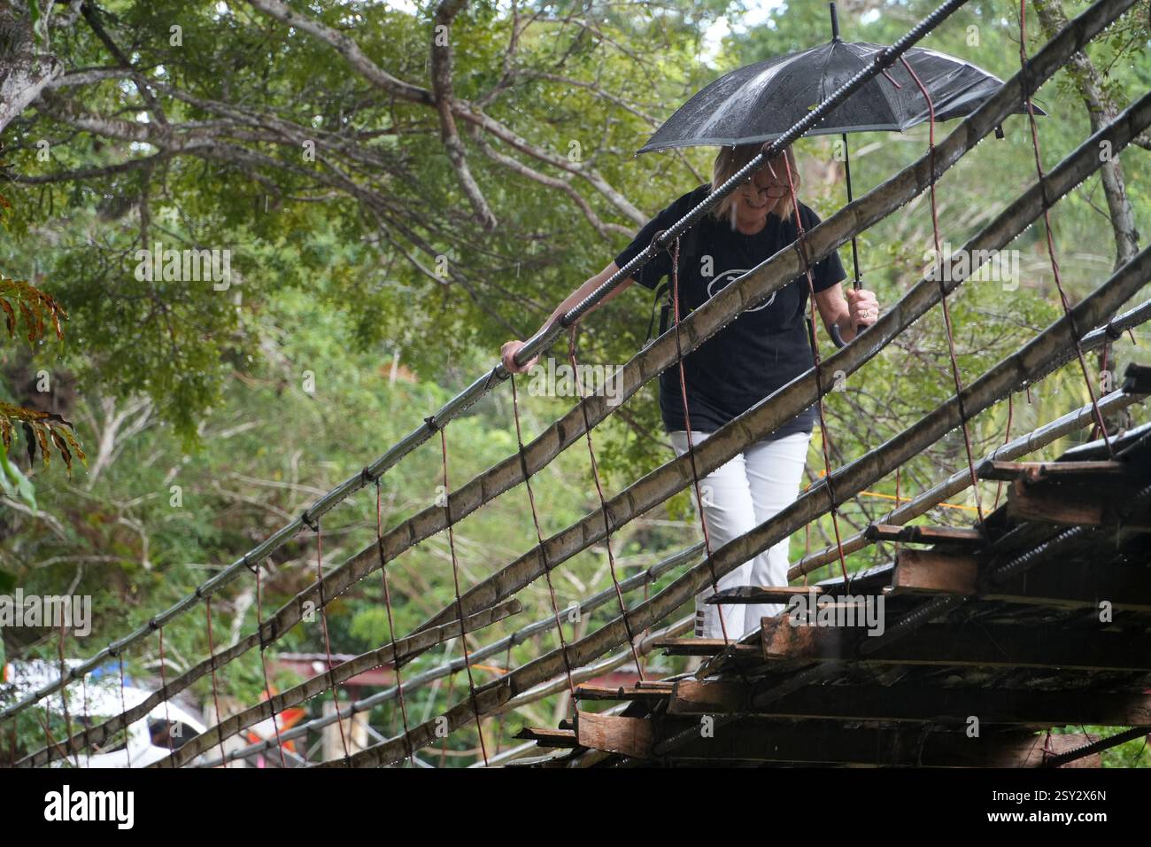 Woman crossing bamboo suspension bridge over a river for pedestrians ...
