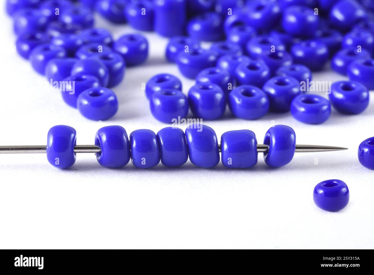 Beads spread on white background with needle. Beads with needle . Close ...