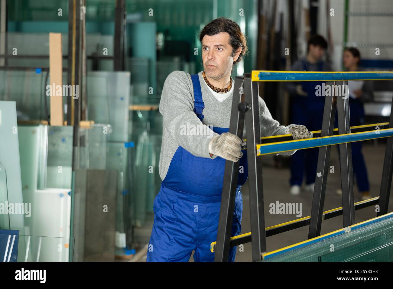 Man glazer employee in blue overall works in glass processing shop ...
