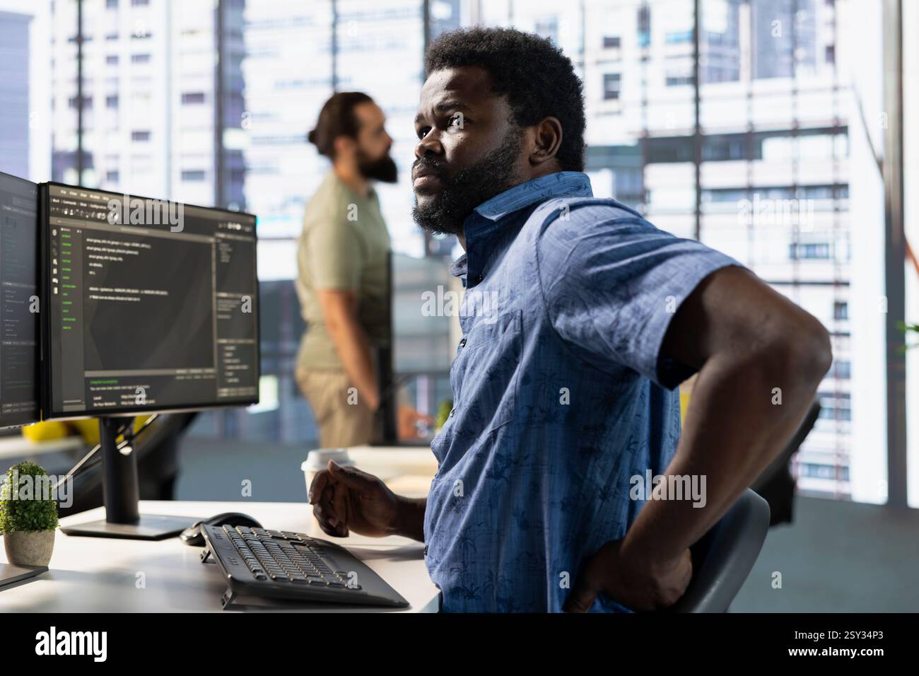 Worker stretching to relieve muscle strain while conducting code review to fix bugs, identifying ...