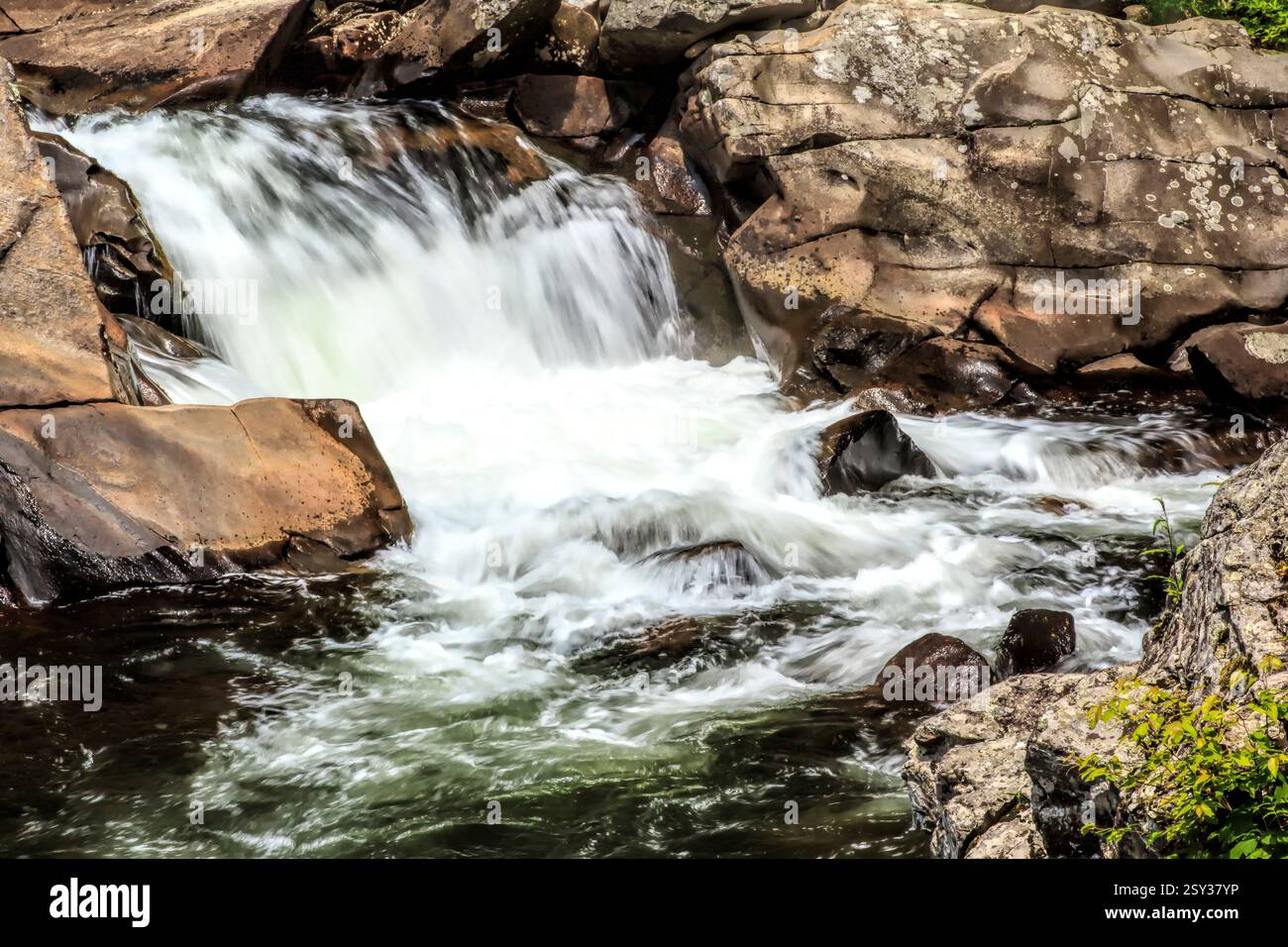 Stream of water is flowing over rocks. The water is clear and has a ...