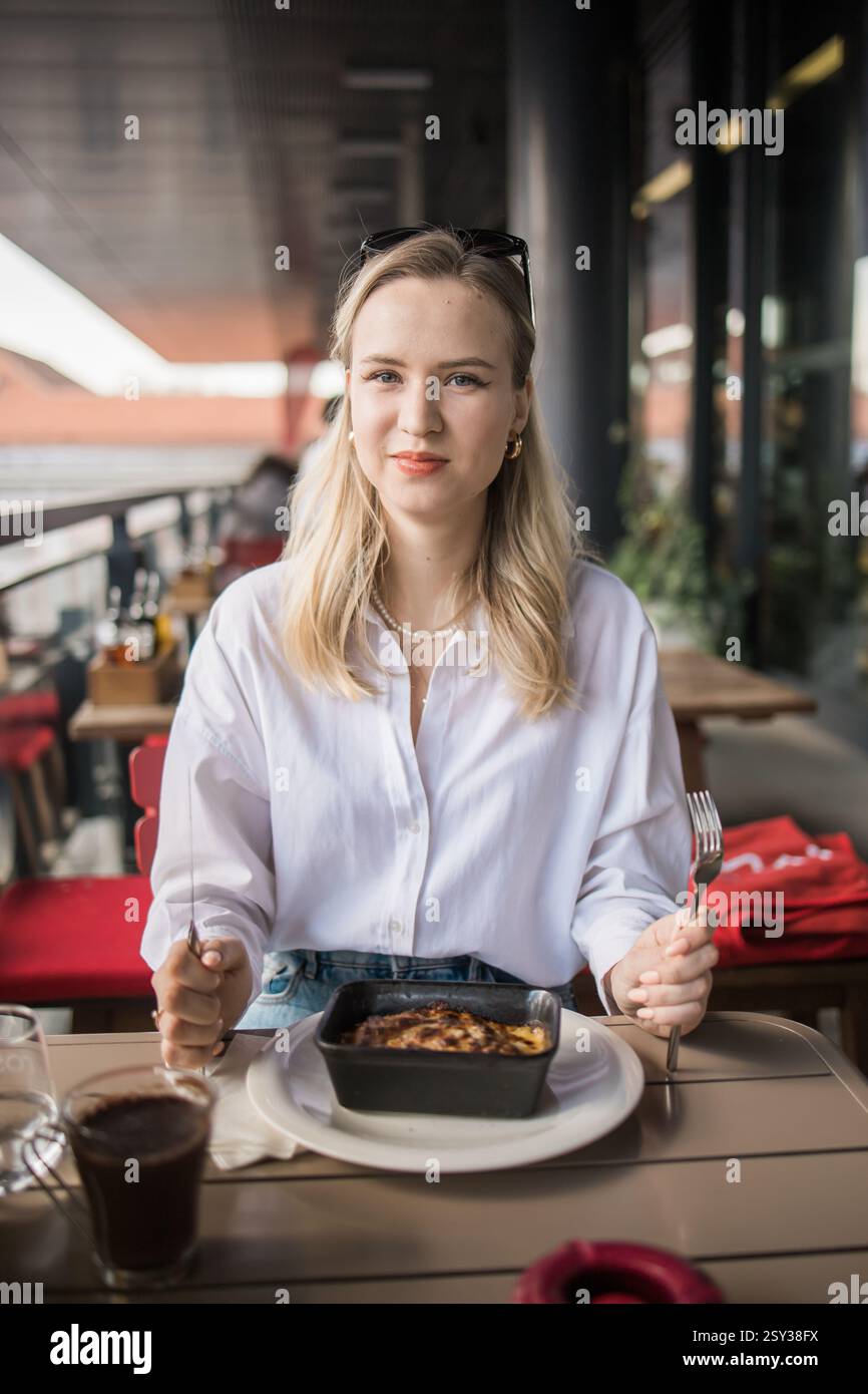 Blonde gen z woman eating lasagna in the cafe on break. Gen z girl ...