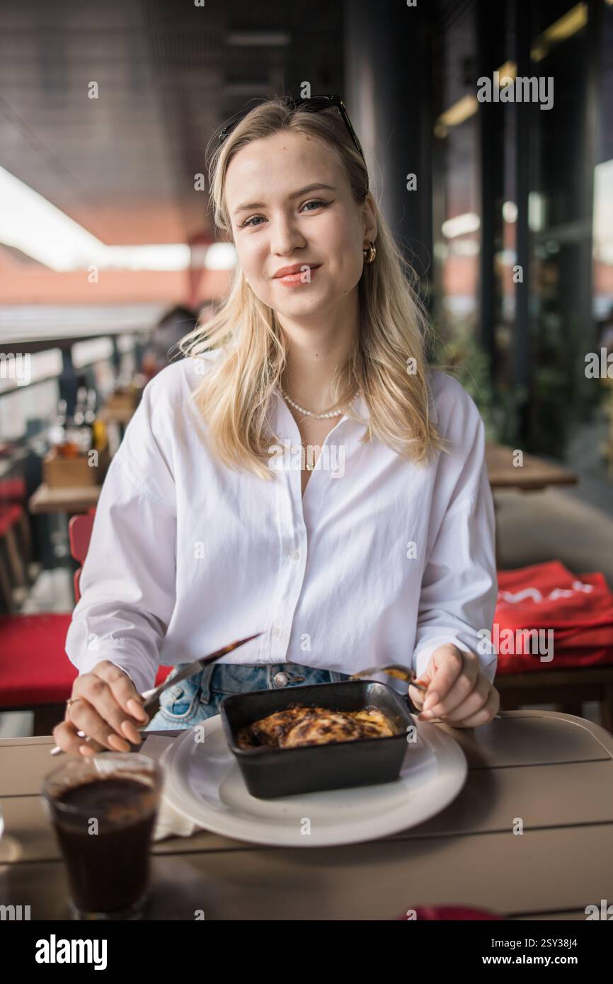 Blonde gen z woman eating lasagna in the cafe on break. Gen z girl ...