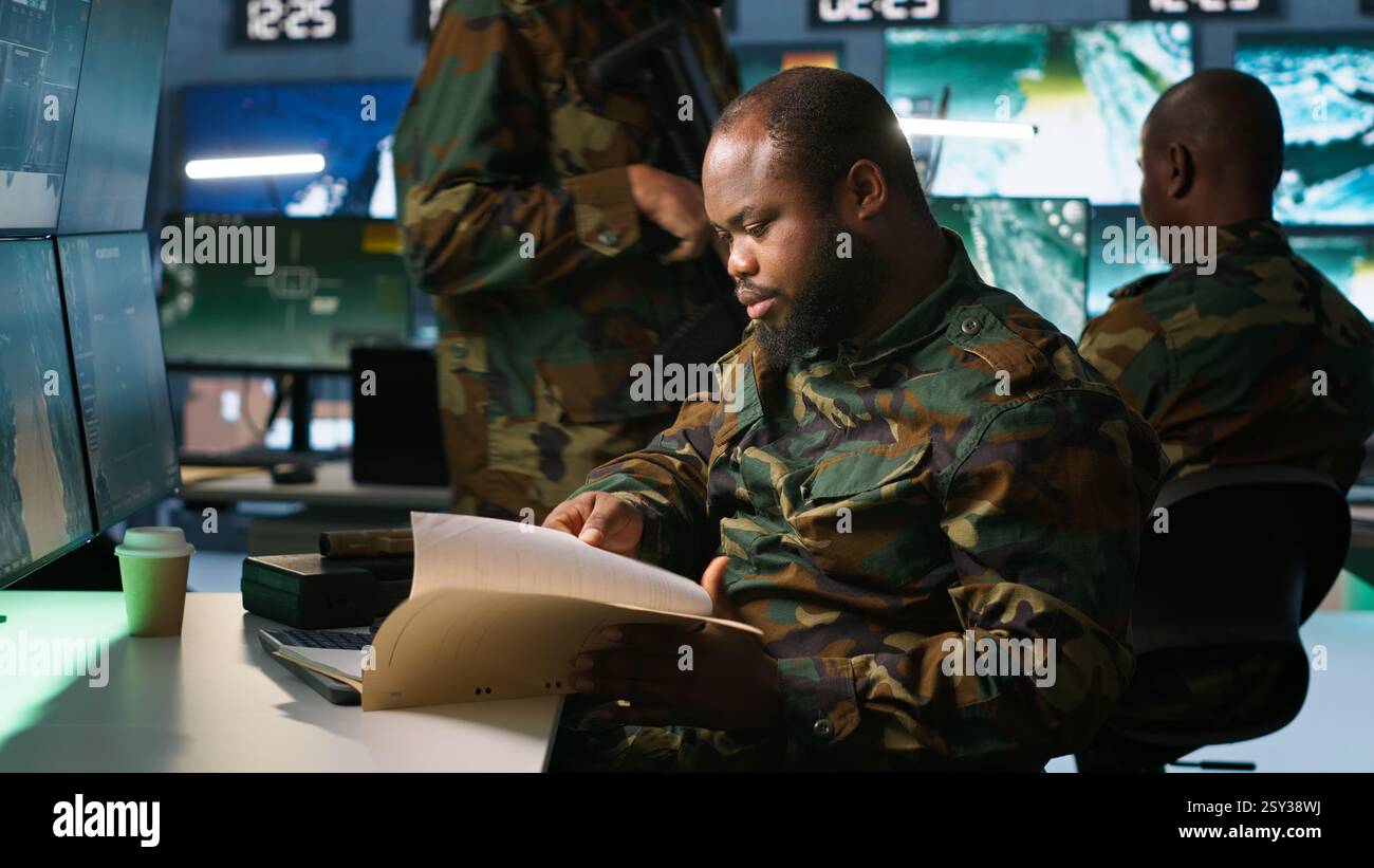 Military soldier in mission control center overseeing national safety operations, reading folder ...