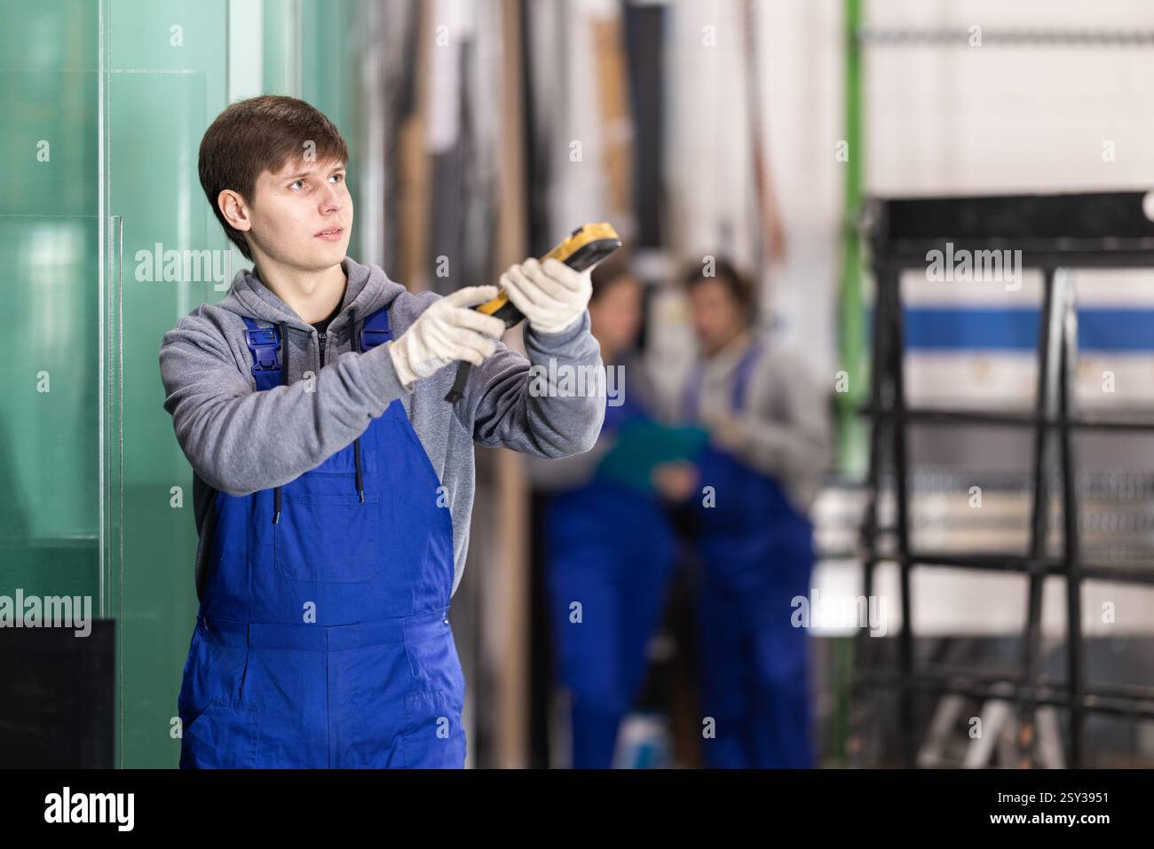 Young man employee in blue overall uses remote control to move lifting ...