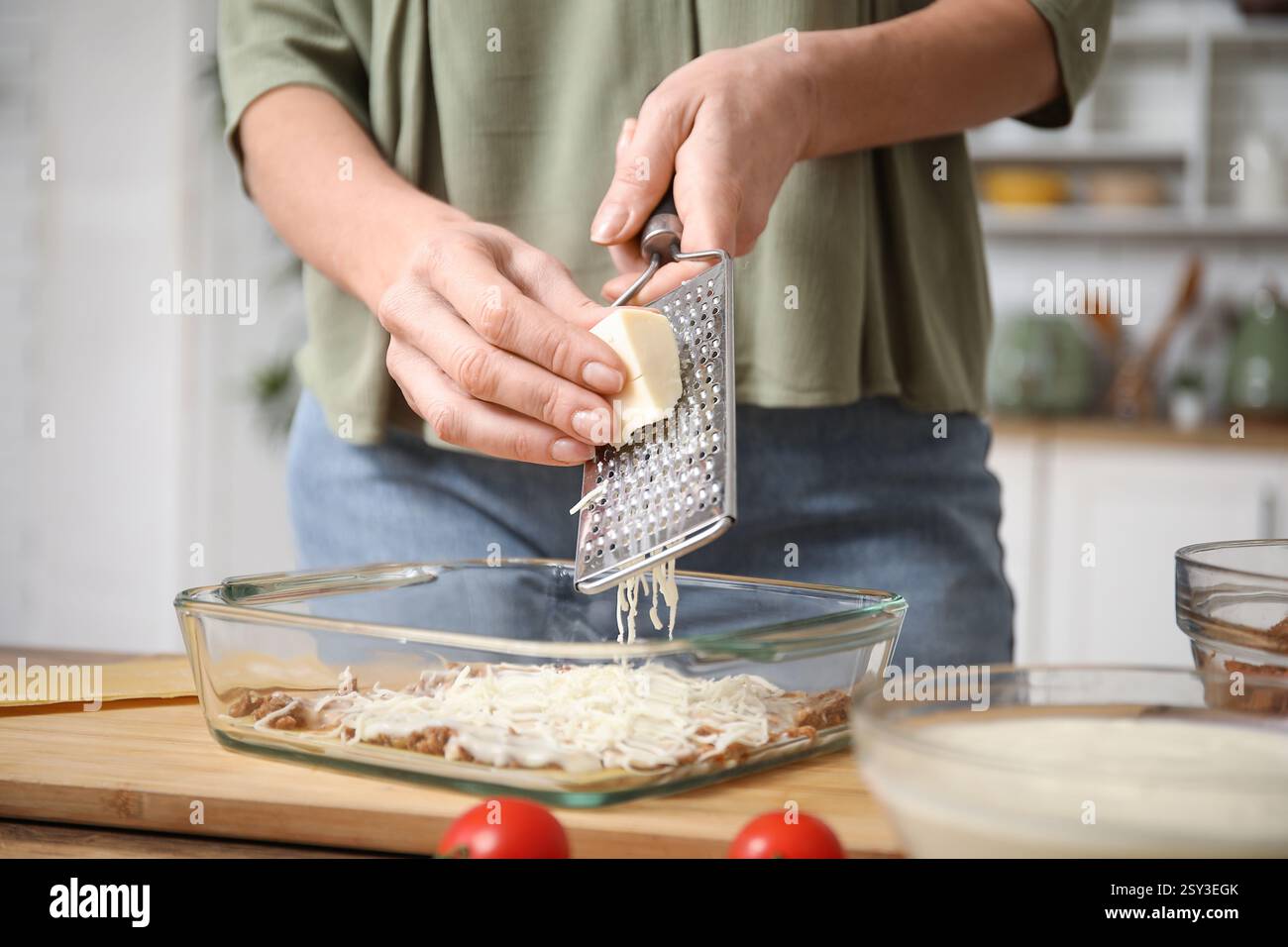 Beautiful mature woman grating cheese for delicious lasagna at table in ...