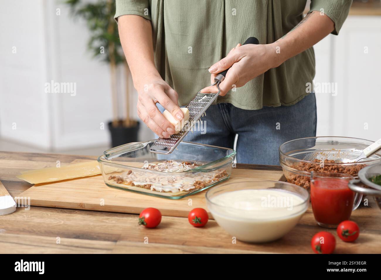Beautiful mature woman grating cheese for delicious lasagna at table in ...