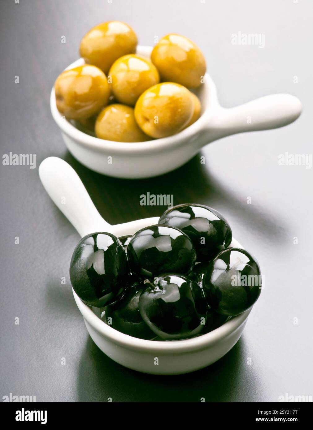 Assorted olives are featured in two small white dishes. One dish ...