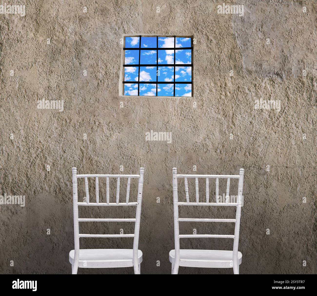 Prison cell with a pair of white chairs under a barred window ...