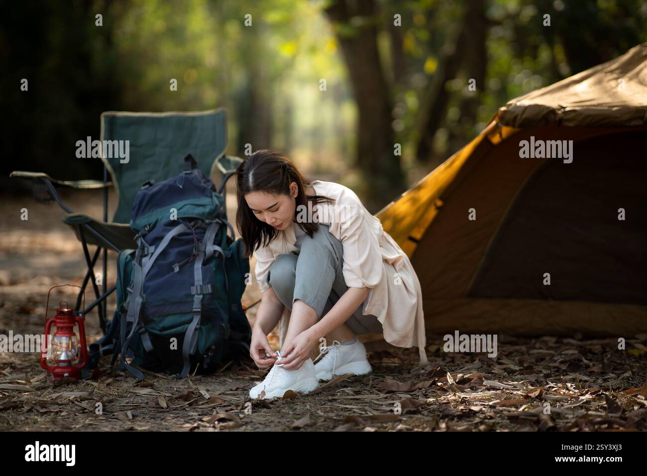 The woman is tying her shoelace in front of the camping tent in the ...