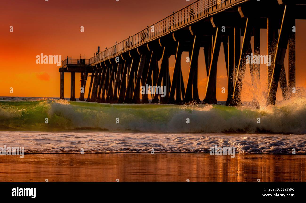 Jade green back lit waves curl up and smash against the pylon of the ...