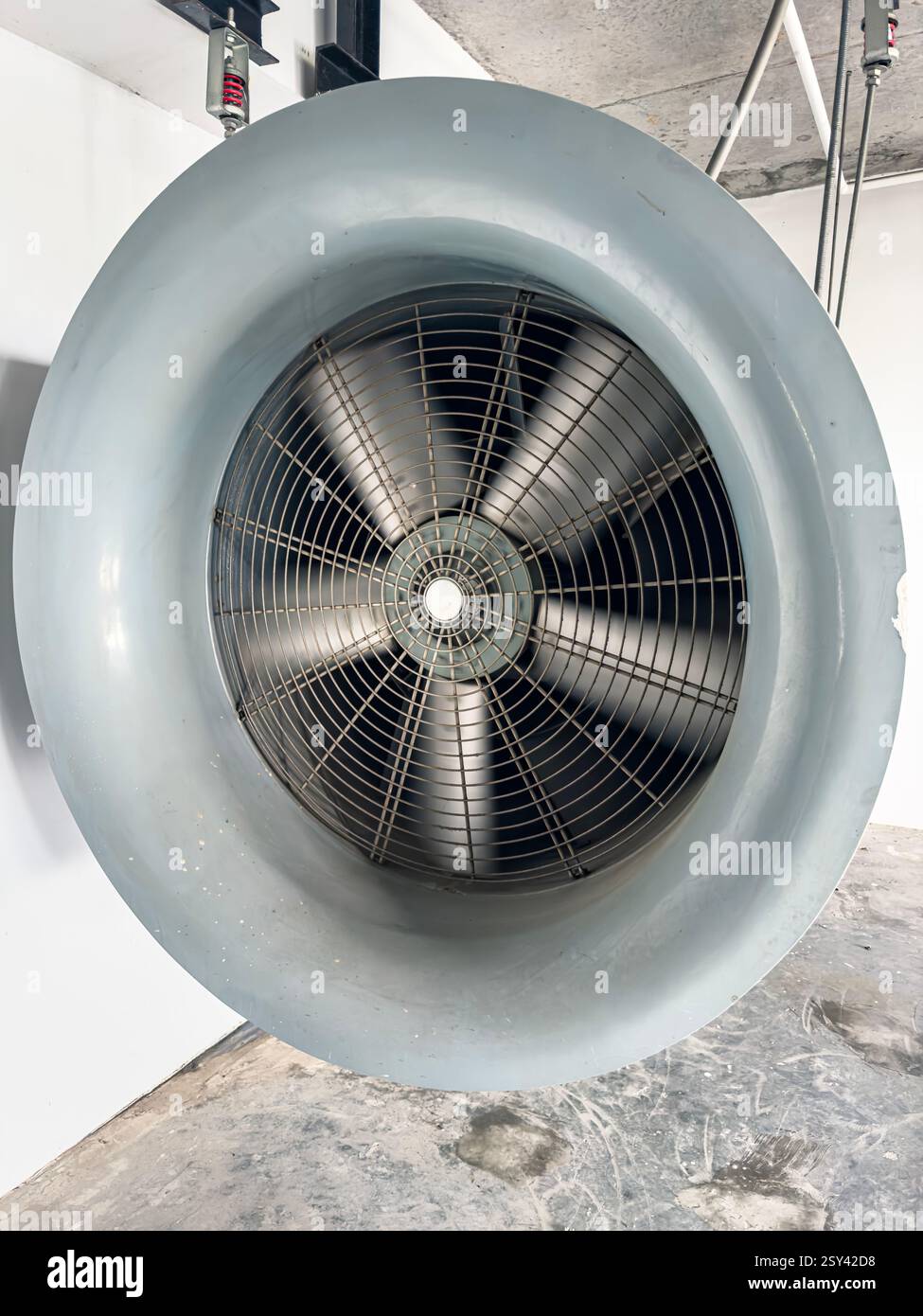 A large, gray, industrial fan is suspended from the ceiling of a ...