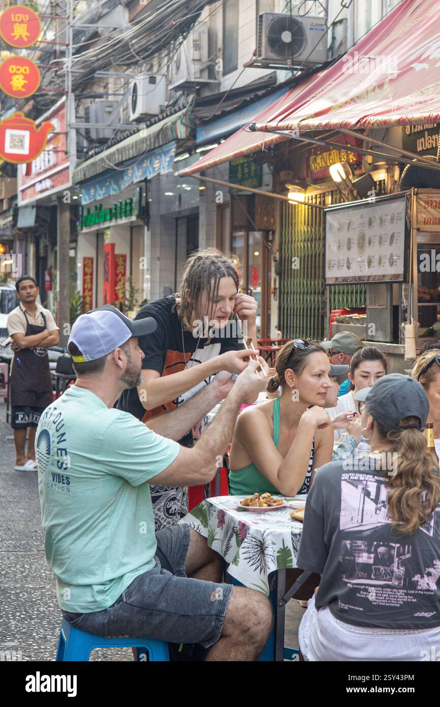 Bangkok, Thailand - FEBRUARY 16, 2025: A group of European tourists enjoy eating street food at ...