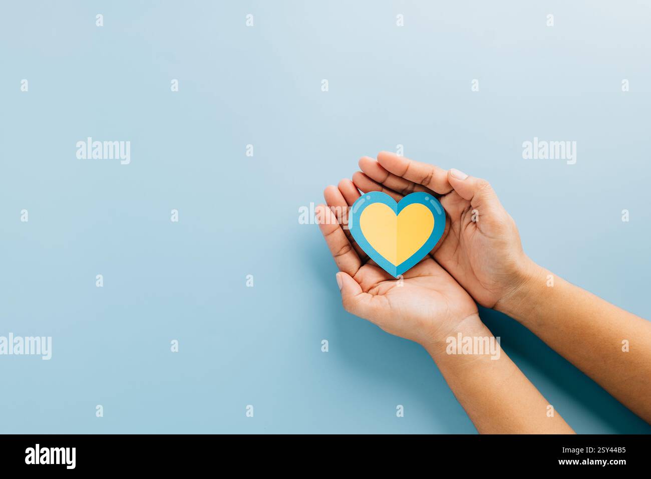 Hands hold a paper heart with yellow inside and a light blue border on ...