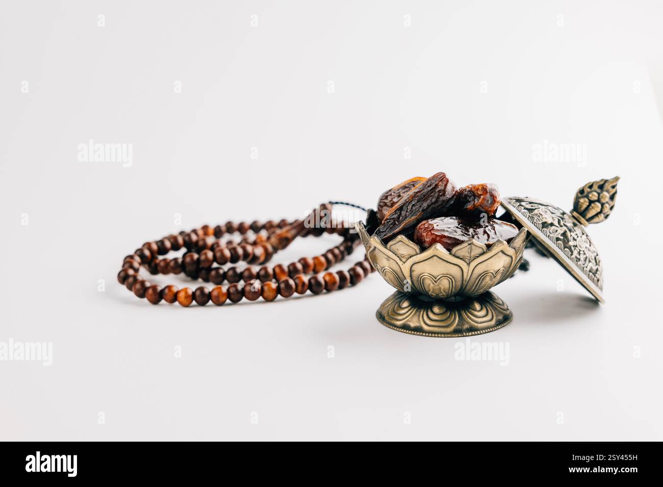 Ornate dish with dates and beads on white background captures Ramadan's ...