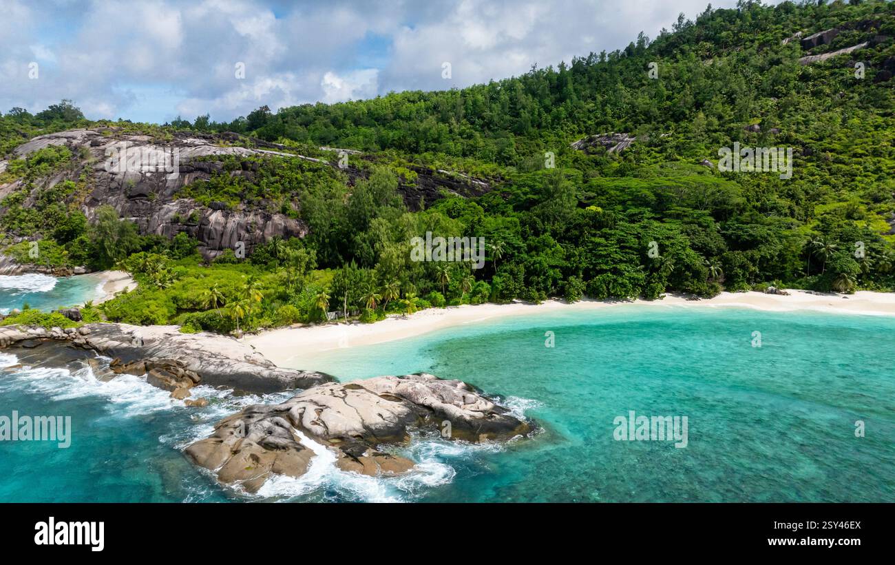 Granite rocks jut out from a pristine white beach, with dense green ...