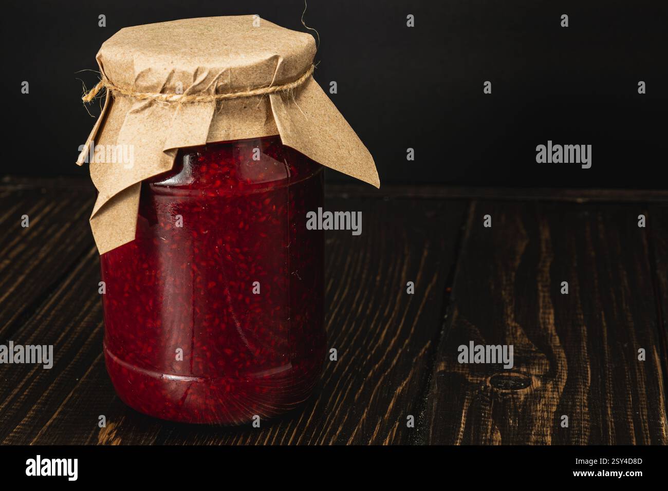 Bright red raspberry and cherry jam fills a large glass jar, topped ...
