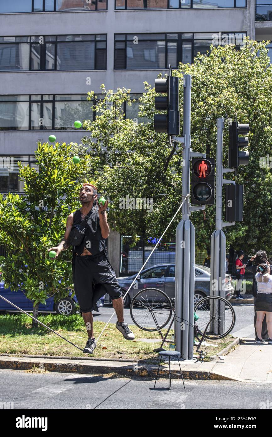 Street artist dances on a rope and juggles between two traffic lights ...